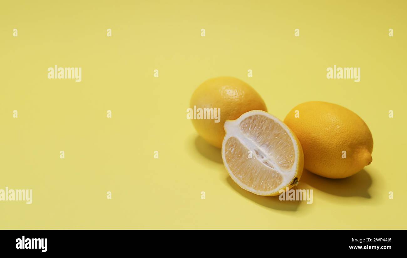 two whole lemons and sliced in half one on yellow background Stock ...