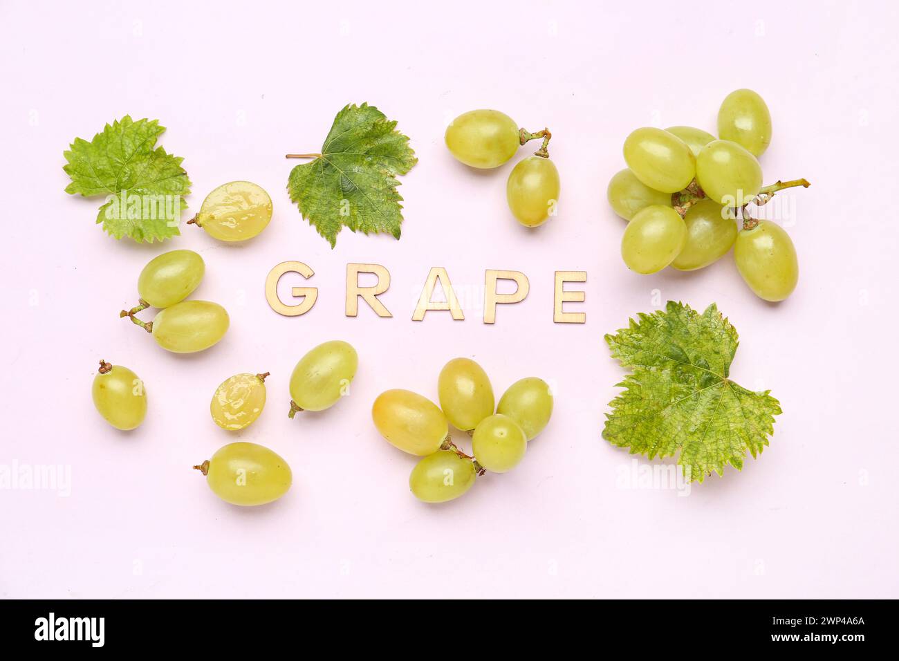 Word GRAPE and fresh green berries with leaves on lilac background ...