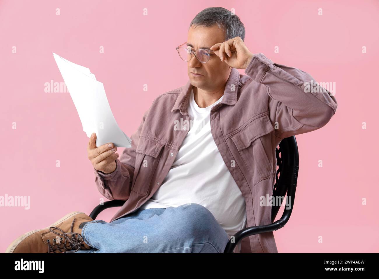 Mature actor reading film script in chair on pink background Stock ...