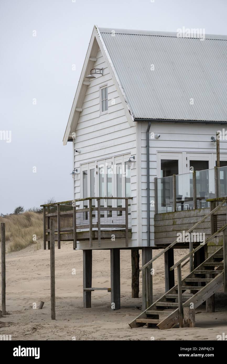 A white beach house built on stilts, elevated in the sand of the dunes ...