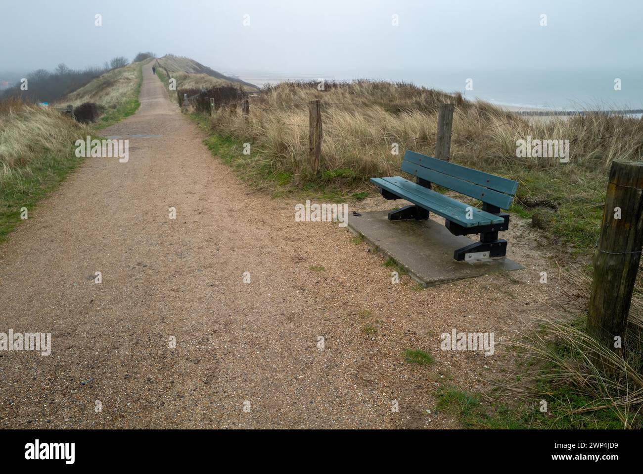 An empty bench on a path with a view of the dunes under a cloudy sky ...