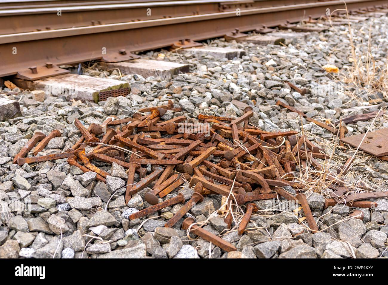 Pile of rusty railroad spikes on crushed stone next to railroad tracks ...