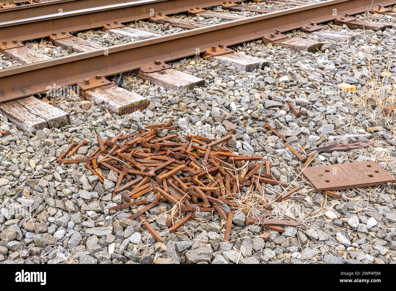 Pile of rusty railroad spikes on crushed stone next to railroad tracks ...