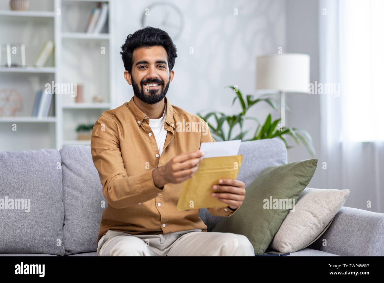 Smiling latino man receiving postal letter and opening it at home while ...