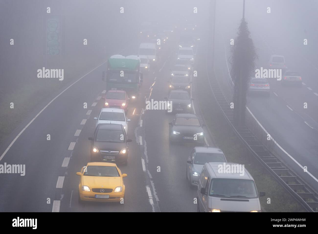 Cars driving on a foggy road with poor visibility in the grey daylight ...