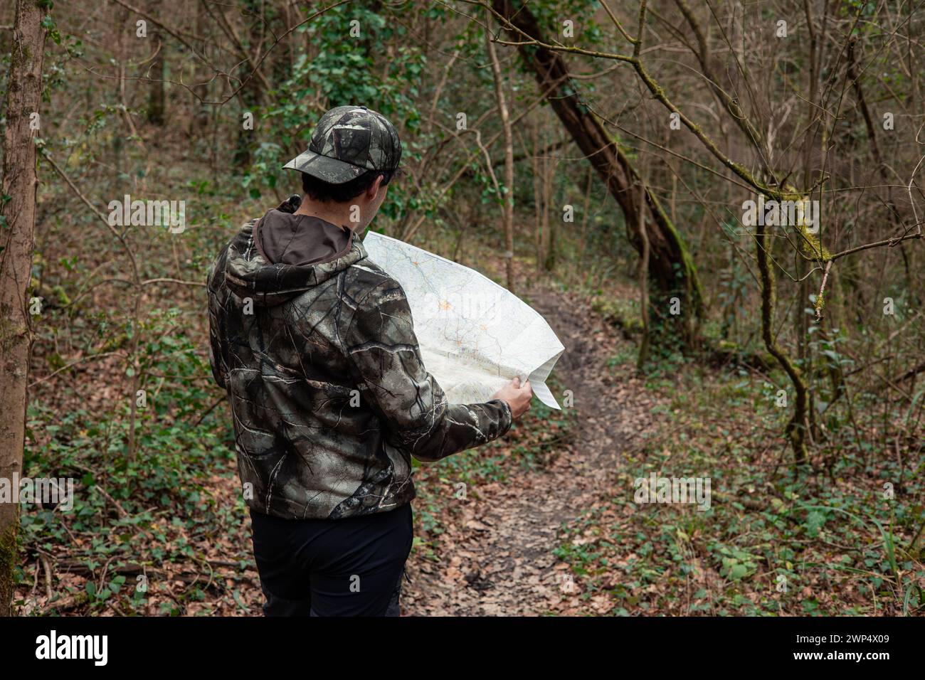 A man in camo, clutching a map, strides down a forest path, venturing ...