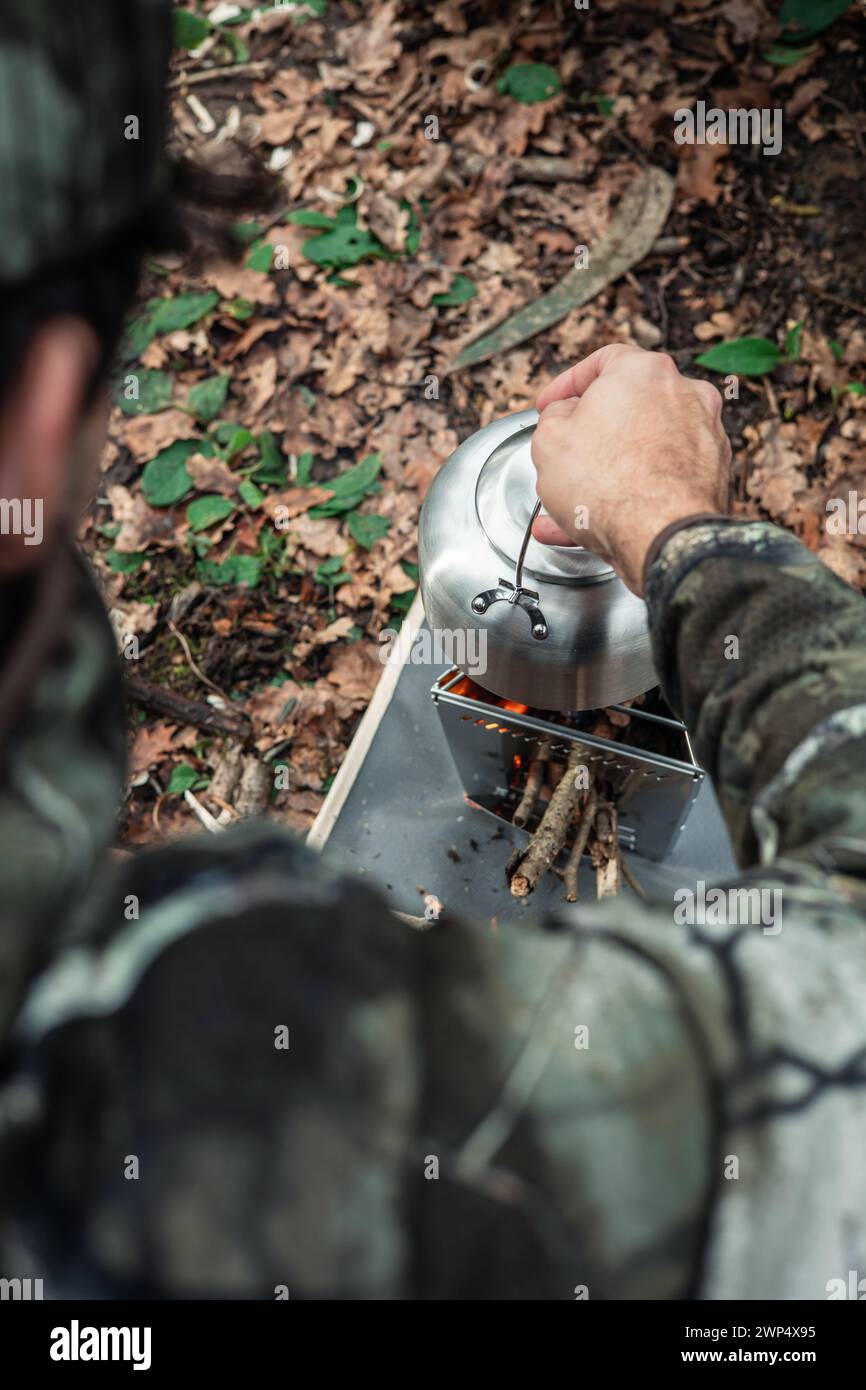 Rear view of an explorer crouching down and placing a kettle on a ...