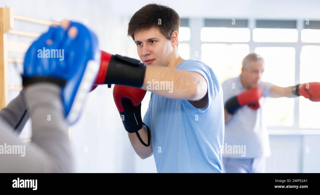 Boxing training - young guy masters boxing strikes on trainer punch ...