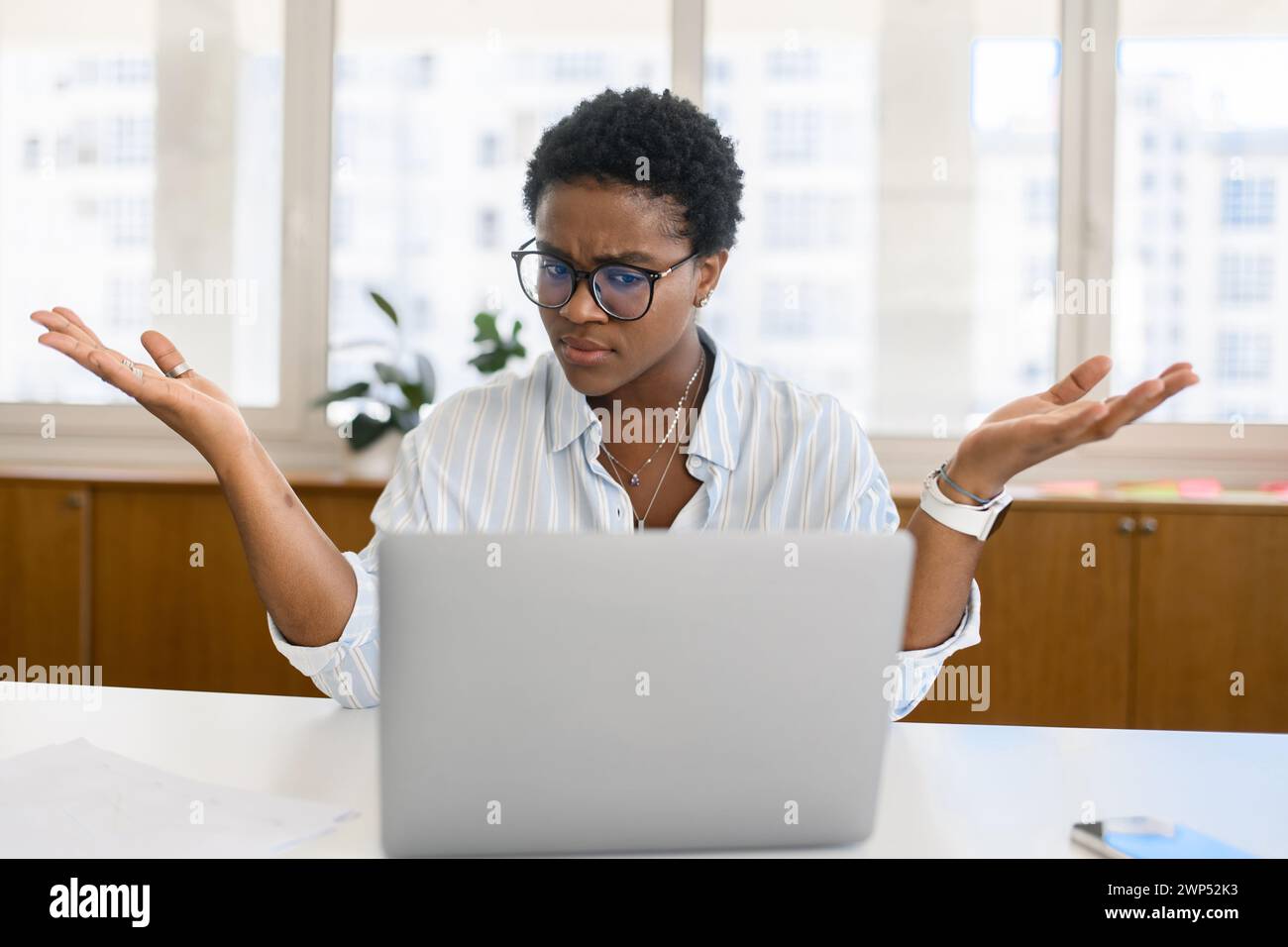 Puzzled African-American female office worker sitting in the workplace ...