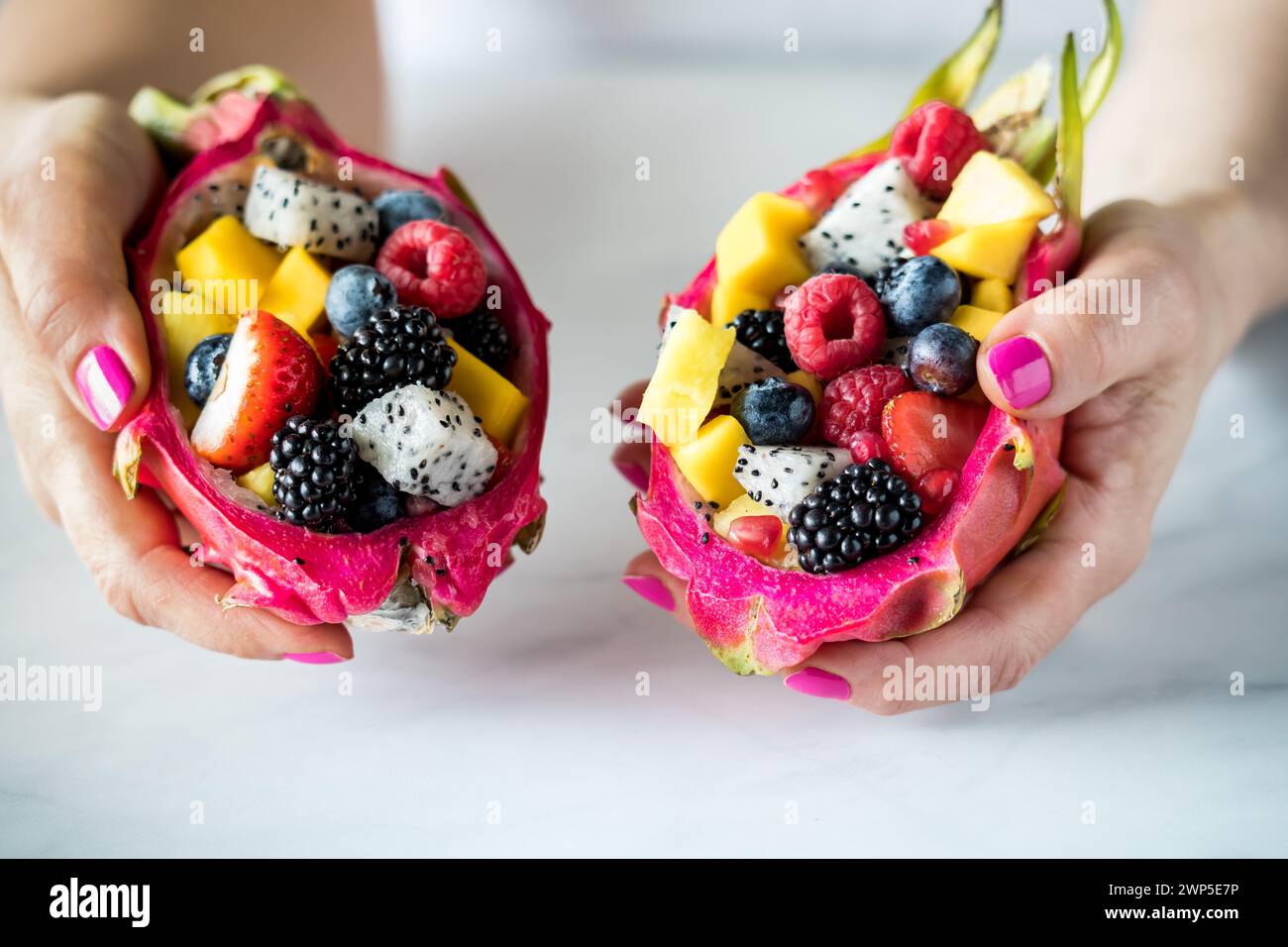 Hands holding dragon fruit shells filled with fresh fruit salad Stock ...