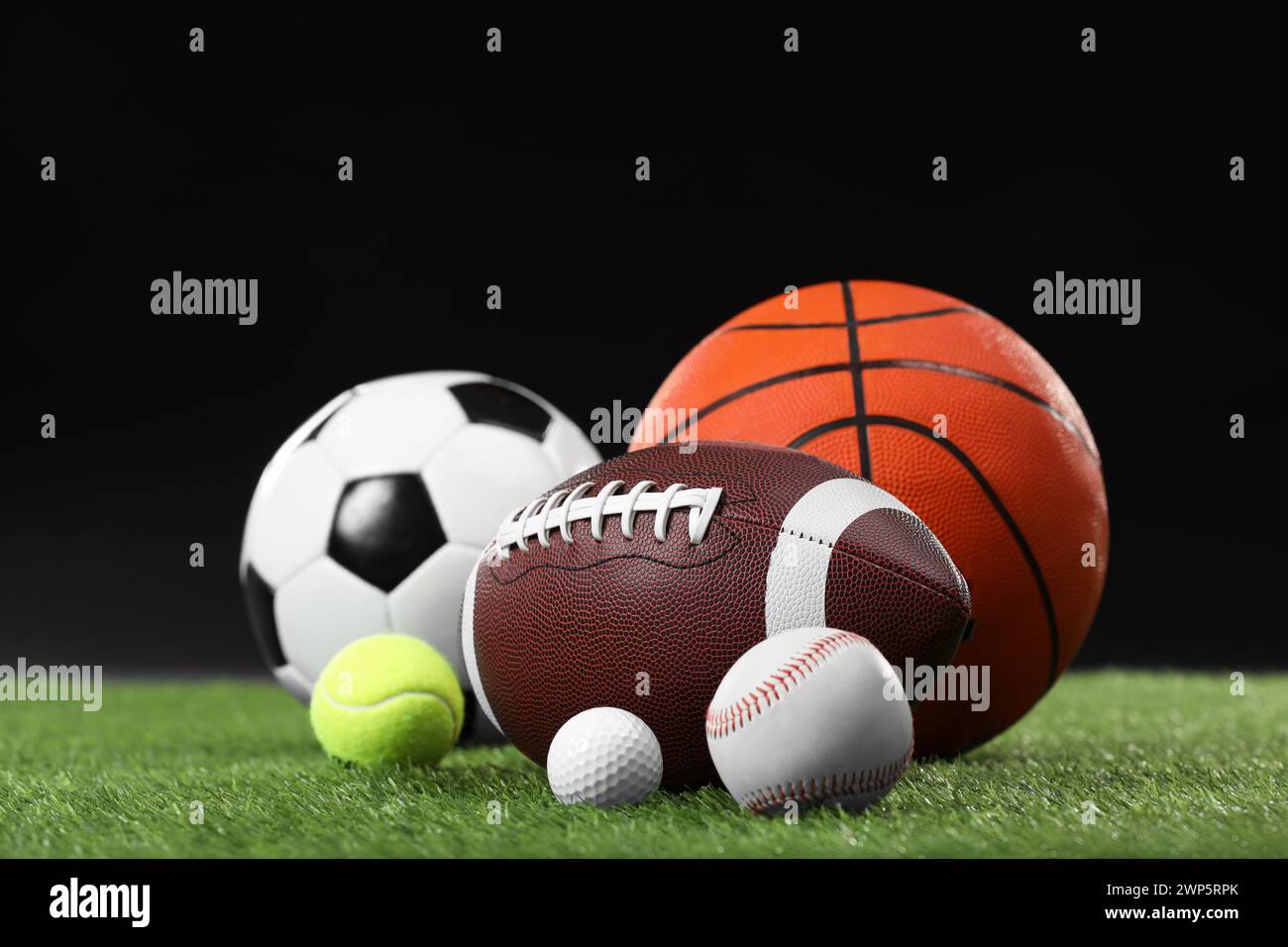 Many different sports balls on green grass against black background ...