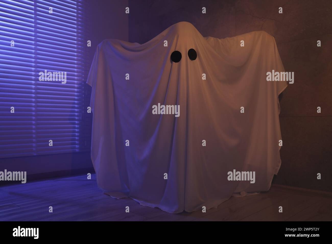 Creepy ghost. Woman covered with sheet near window in color lights ...