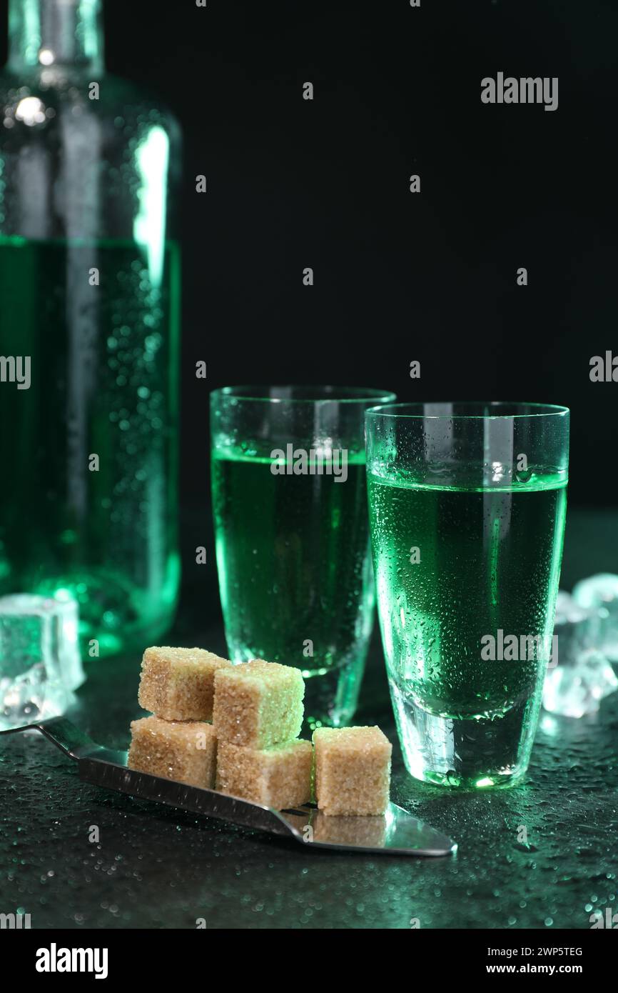 Absinthe in shot glasses, brown sugar cubes and spoon on gray table ...