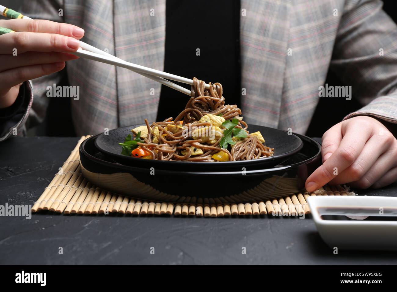 Stir-fry. Woman eating tasty noodles with meat and vegetables at dark ...