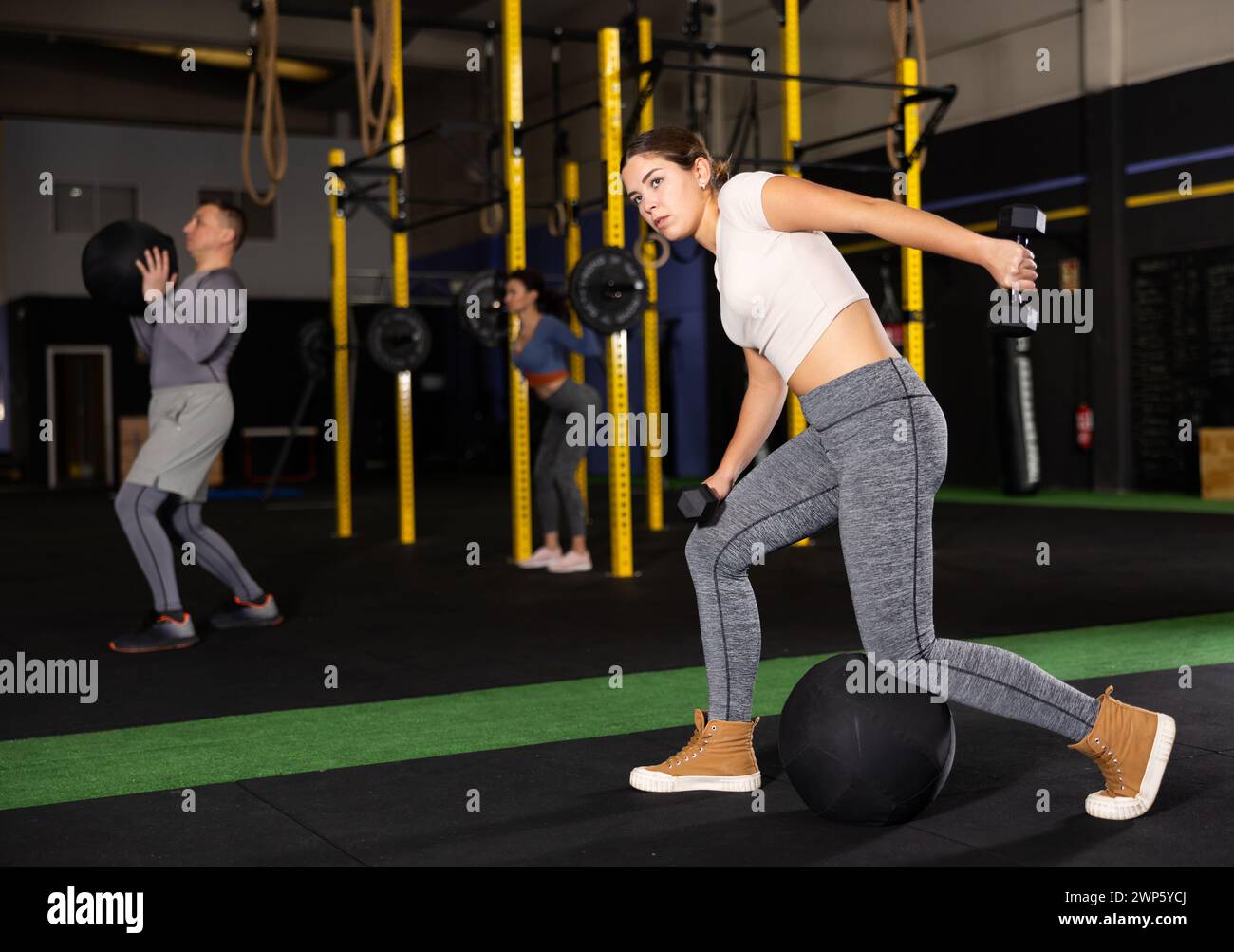 Slender girl trains muscles of arms and back using dumb-bell shaped ...