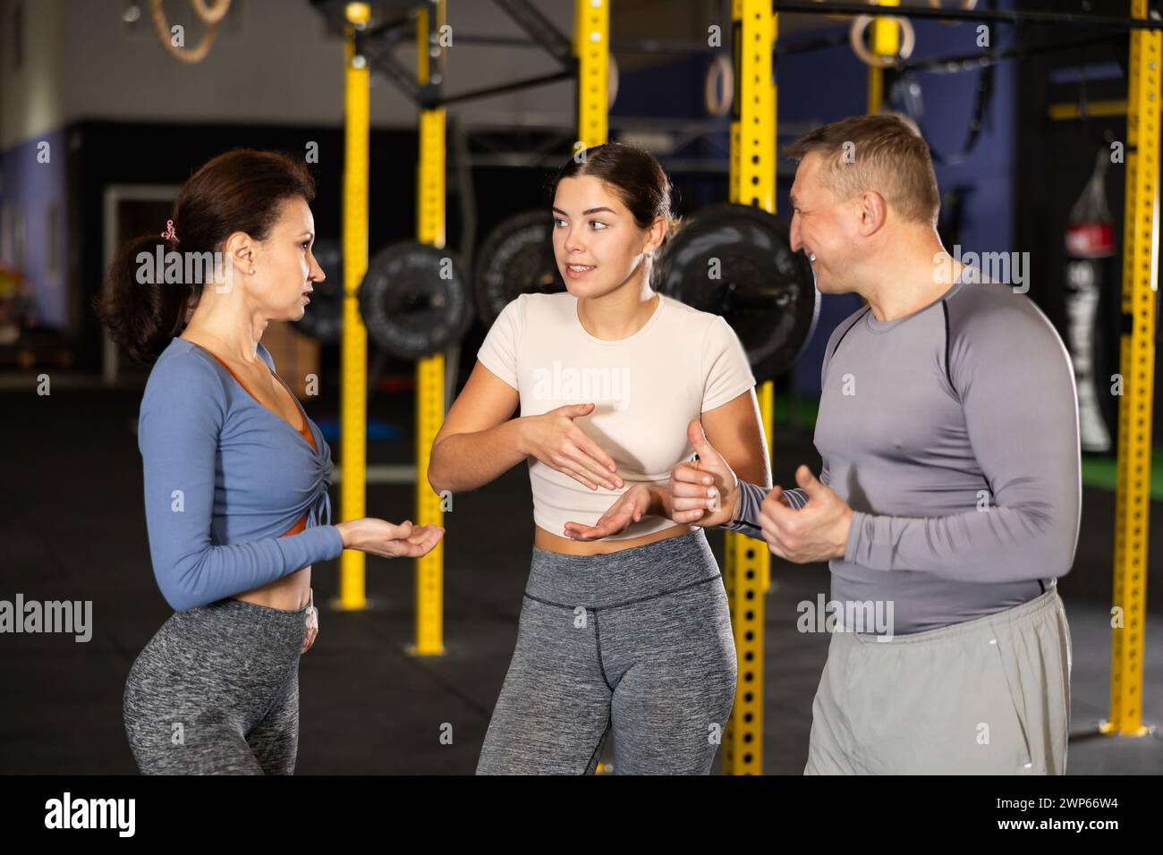 Friendly gym trainer talking to interested female clients Stock Photo ...