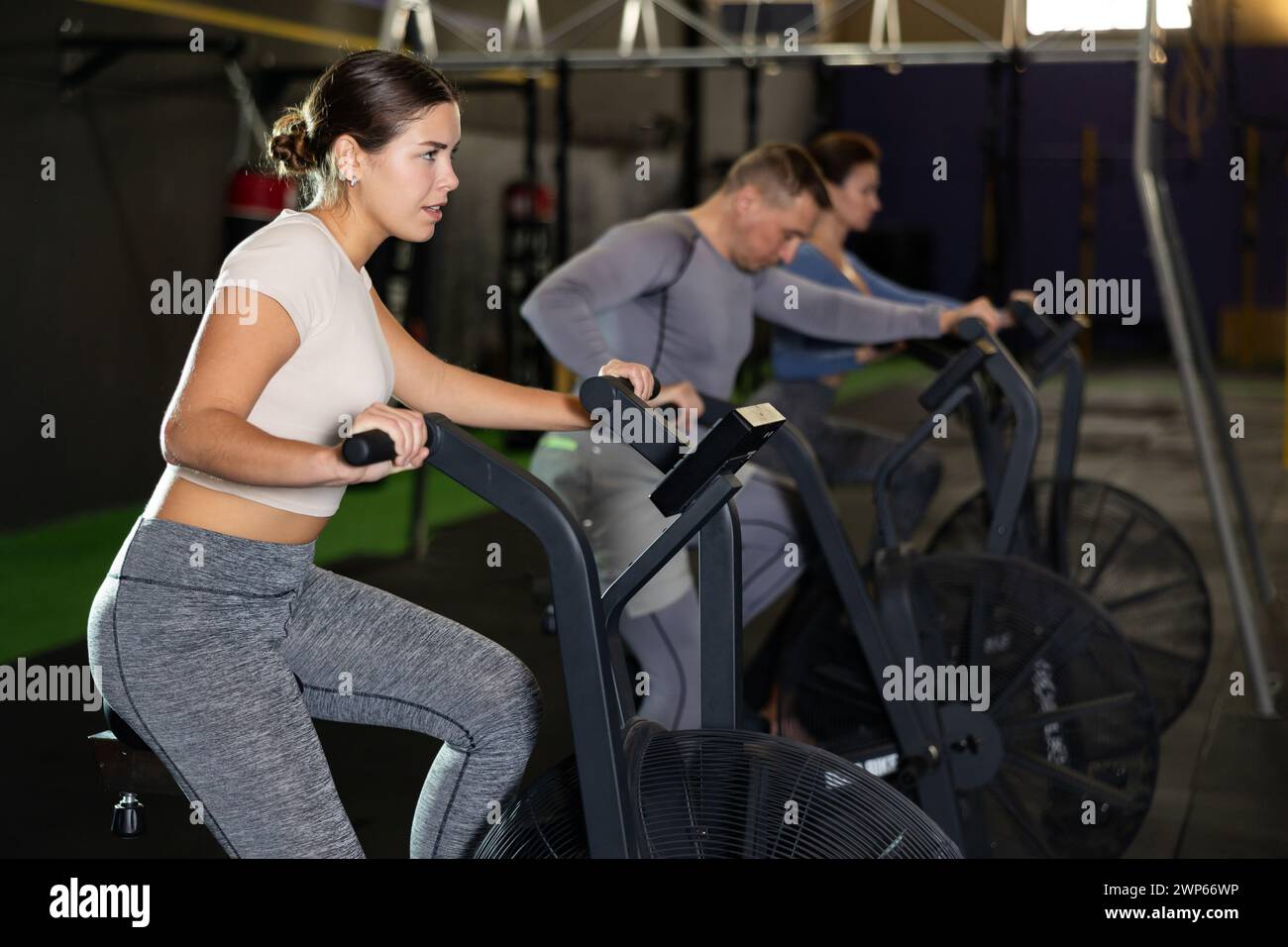 Girl intensely working out on stationary air bicycle in gym Stock Photo - Alamy