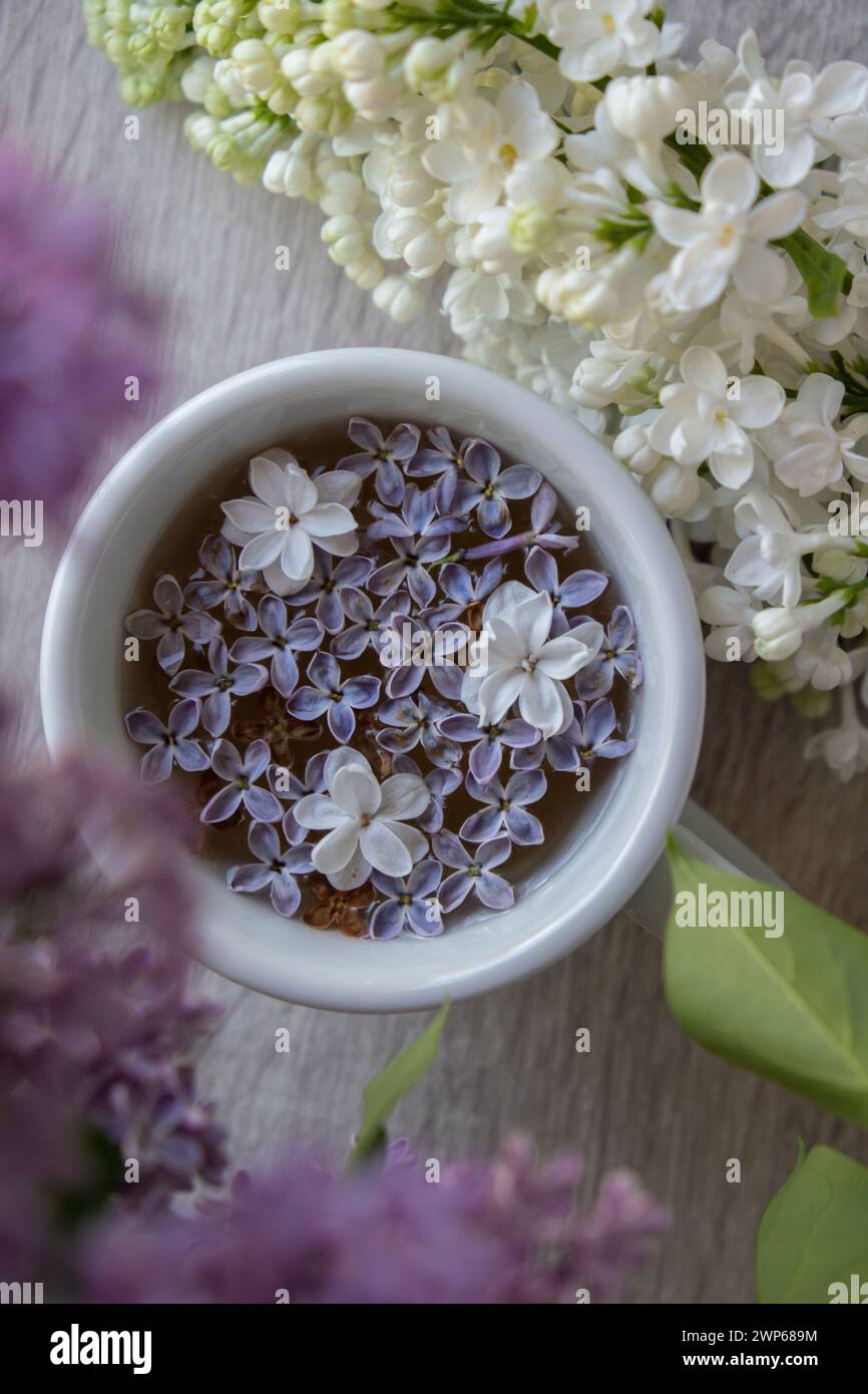Tasty black tea in white cup on windowsill with aromatic lilac flowers ...