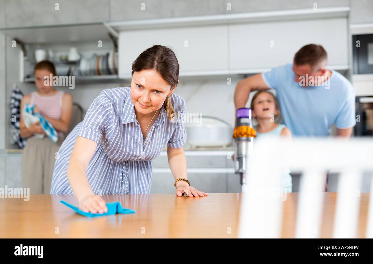 Wife cleans table with rag, husband and children clean kitchen in ...