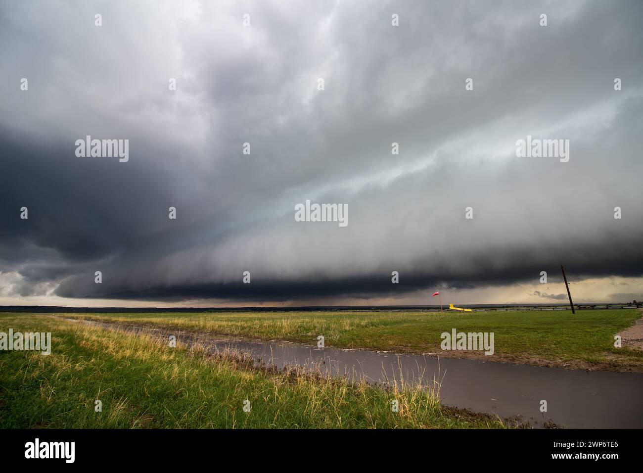 A long roll cloud in the sky, aligned parallel to a water filled ditch ...