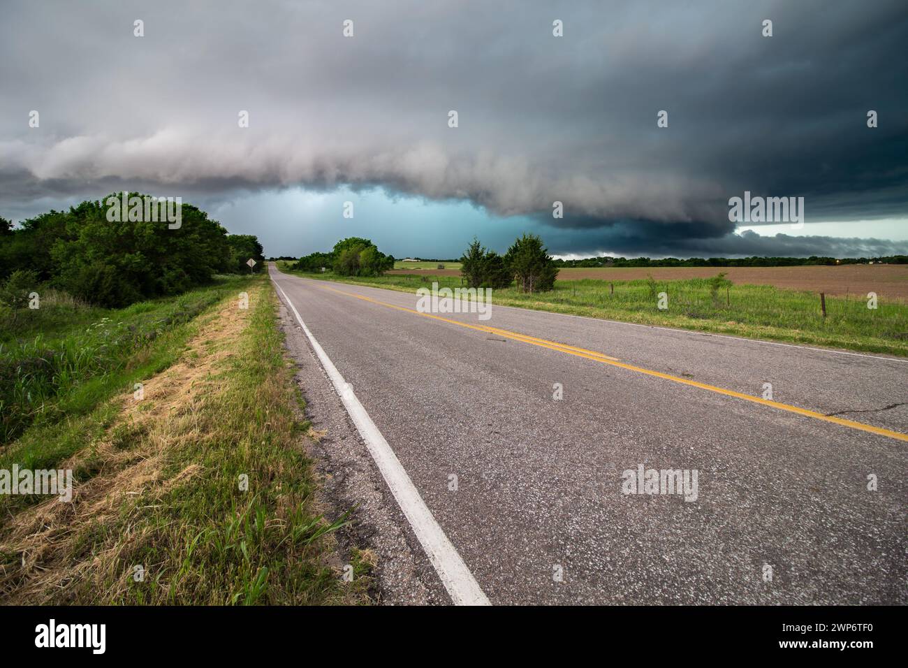 An empty road leads into a severe thunderstorm with a low shelf cloud ...