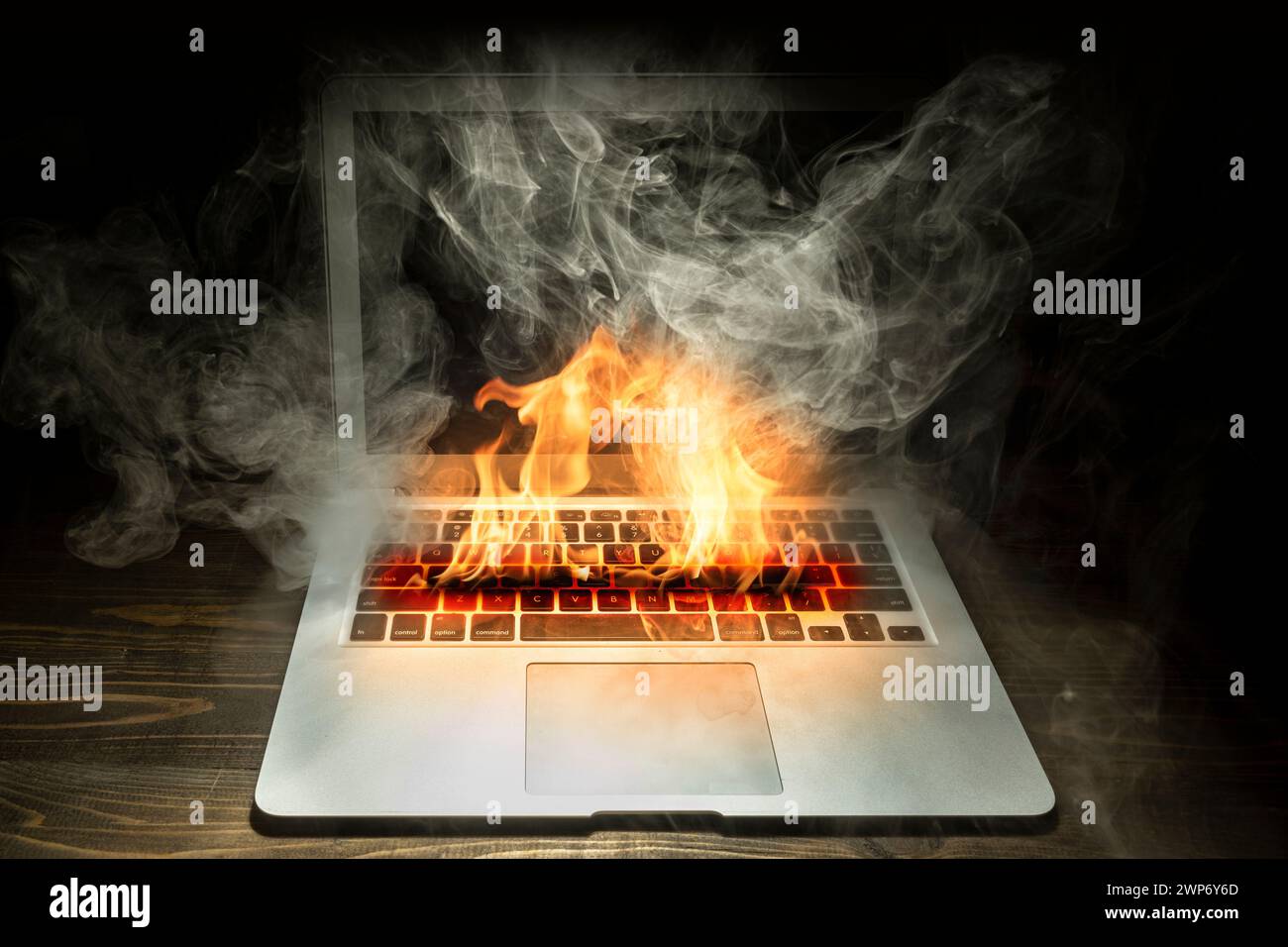 Close up laptop burned with flame and smokes on a wooden desk isolated ...