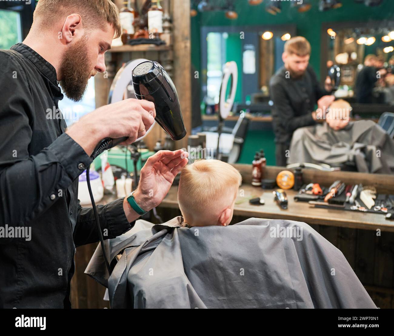 Competent barber styling fresh haircut. Back view of little boy getting ...