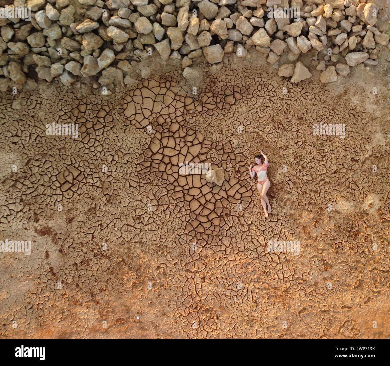 Aerial portrait of beautiful young lady in bikini lying on dry cracked ...