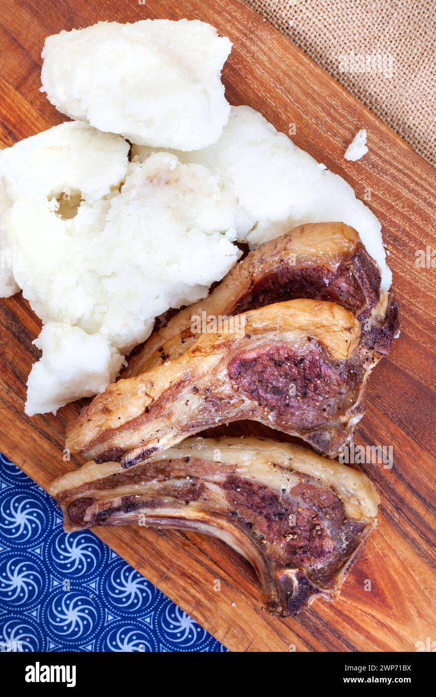 three lamb rib chops with pap or maize meal on rustic chopping board ...