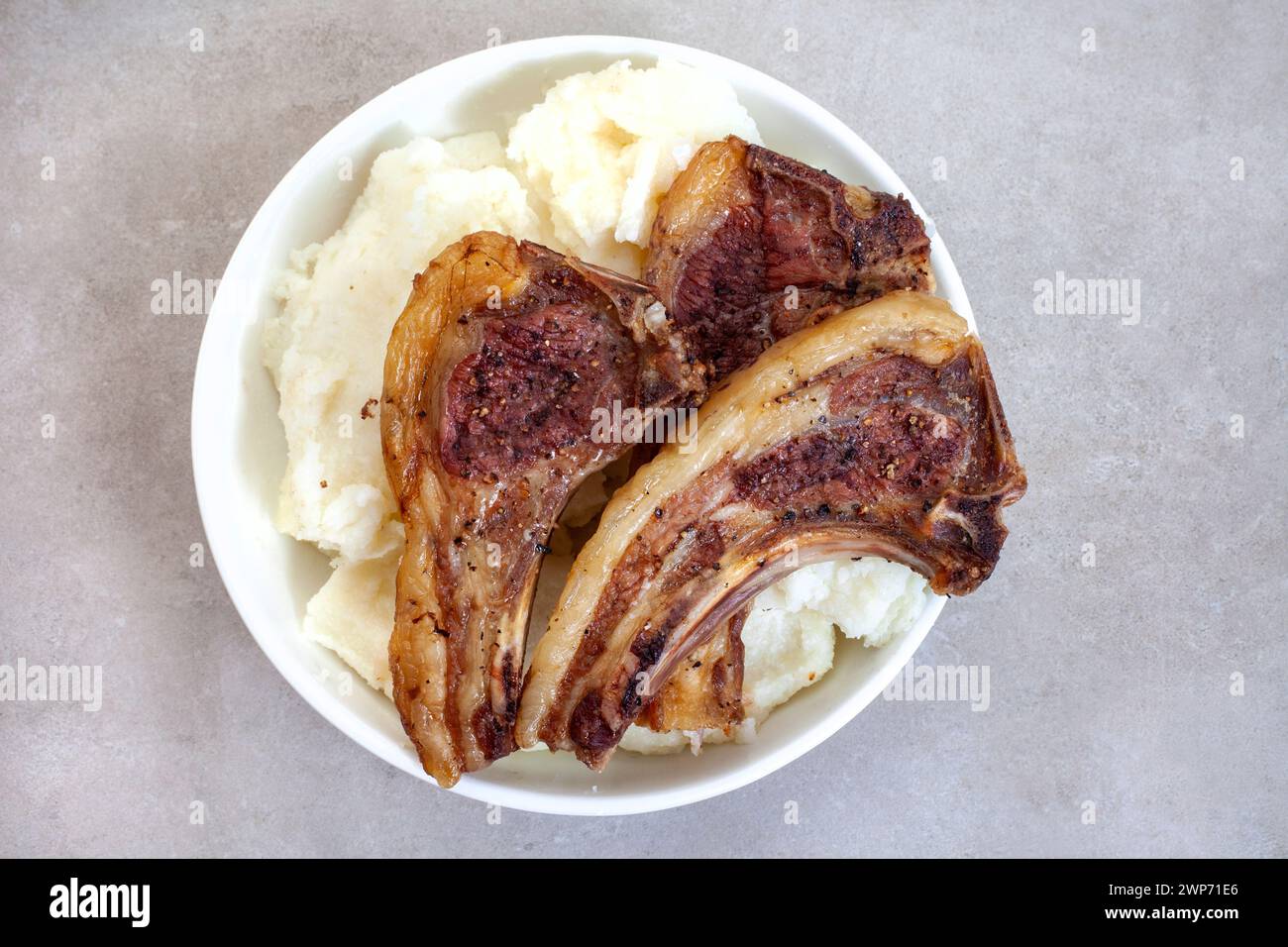 three lamb rib chops with pap or maize meal on a mottled grey ...