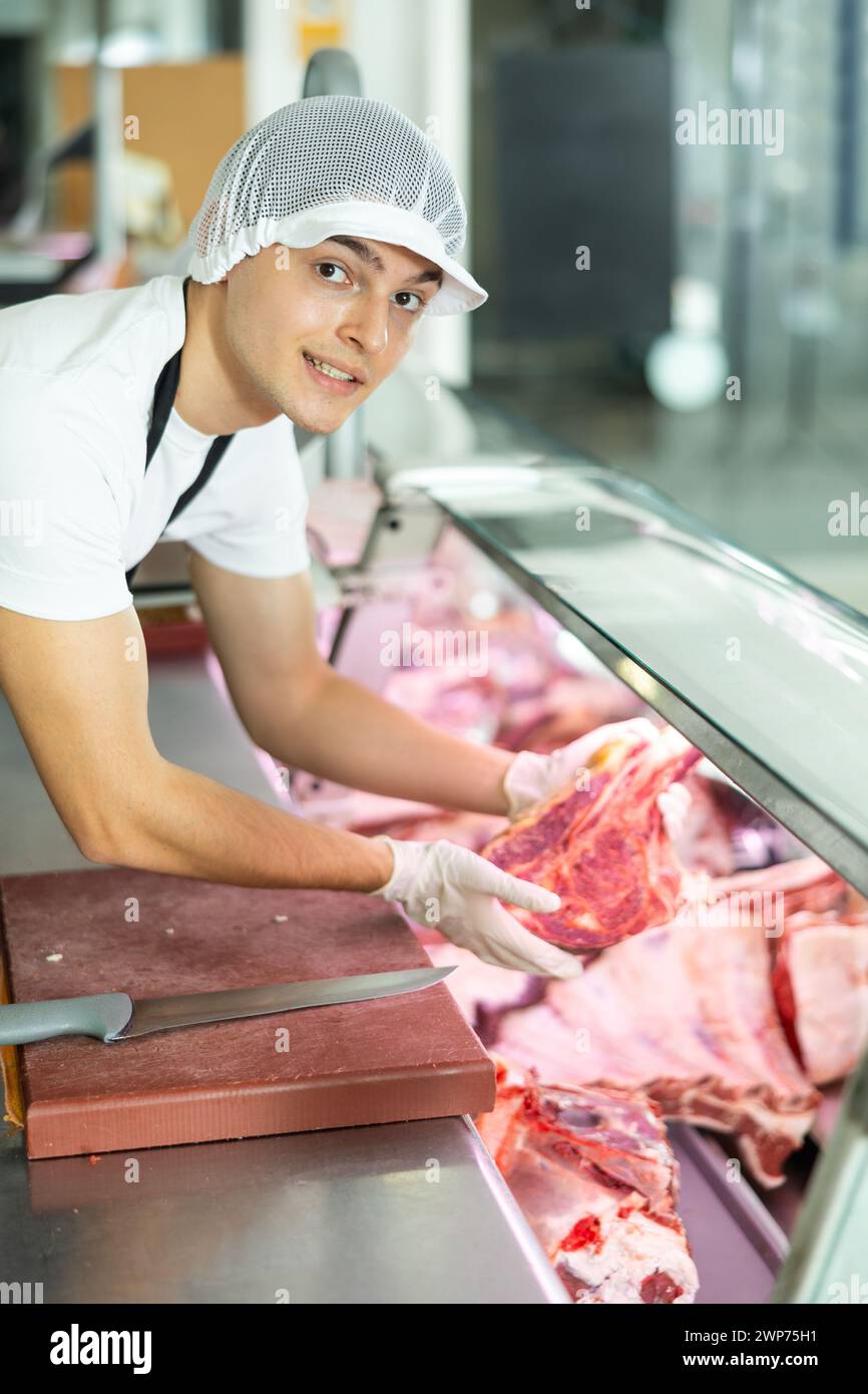Positive Young Salesman Demonstrating Piece Of Meat In Butcher Shop