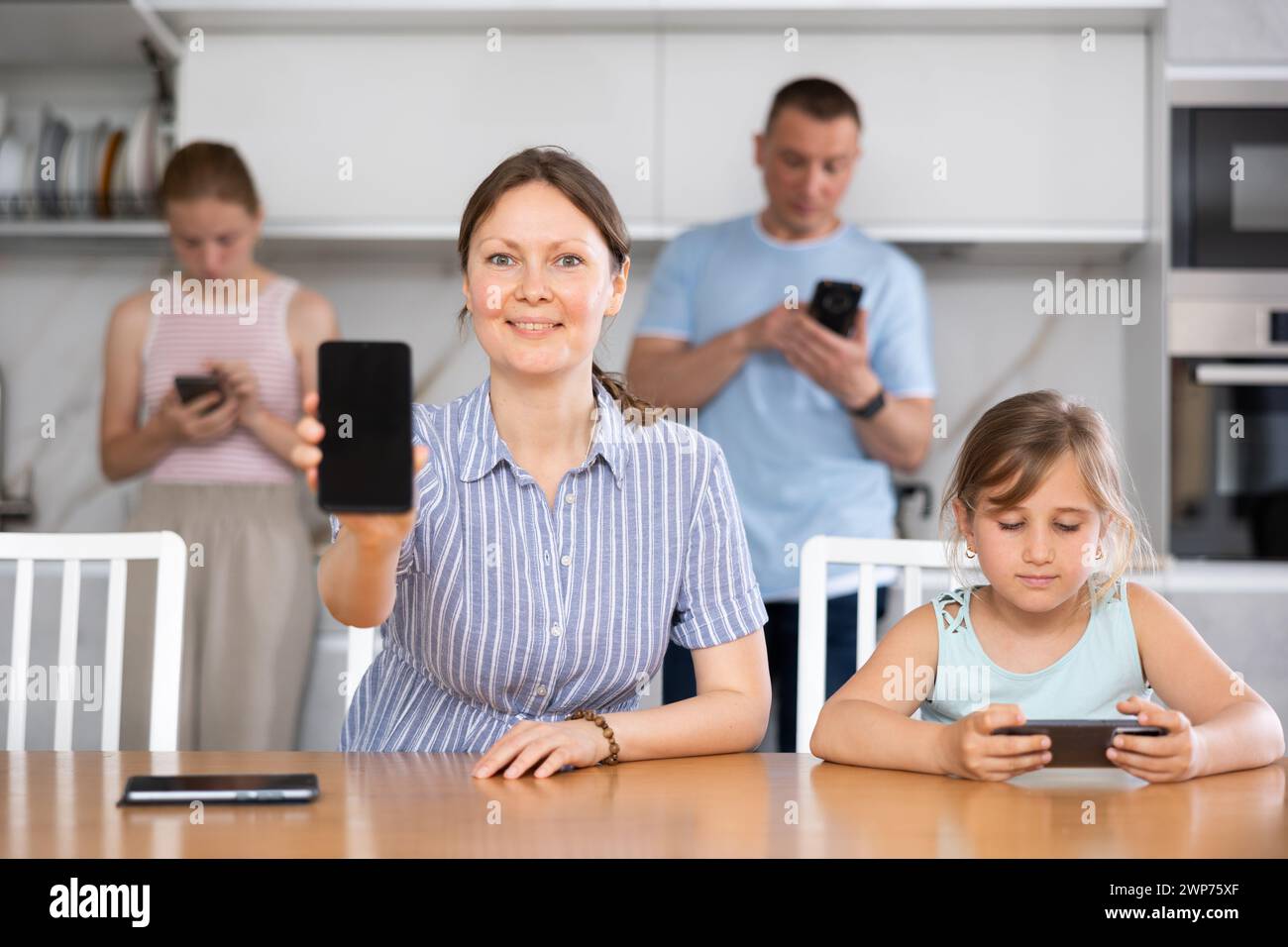 Mom showing the screen of her phone. Children and husband typing on ...