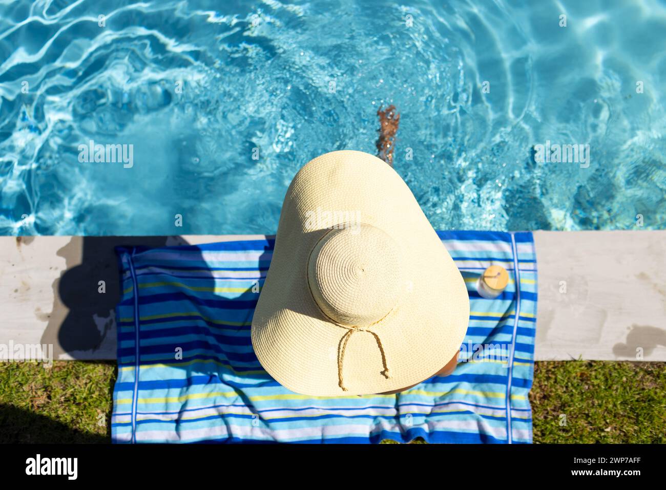 A woman relaxes on a striped blue towel by a shimmering pool, wearing a ...