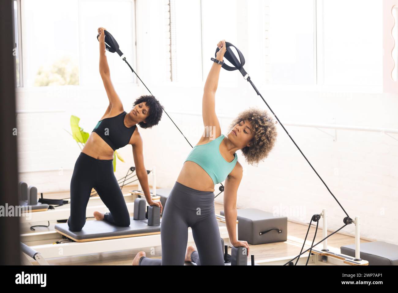 Biracial women exercising at a fitness studio on Pilates reformers ...