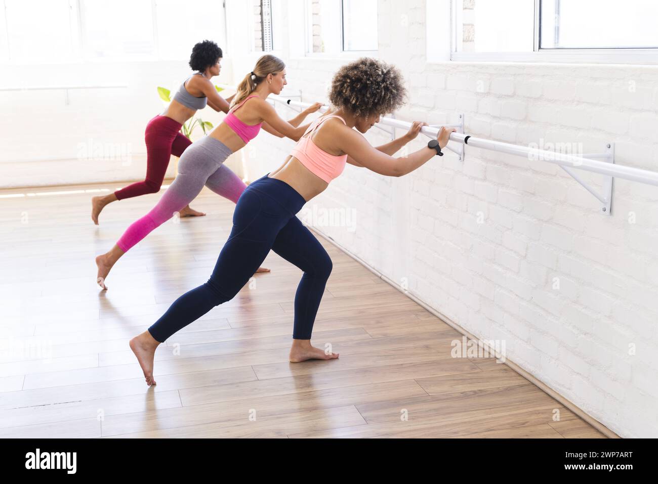 Diverse women engage in a barre workout at a studio. The session ...