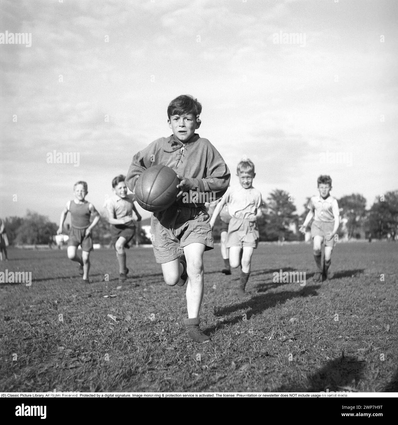 Rugby 1940. Young rugby players practise together. The boy running with ...