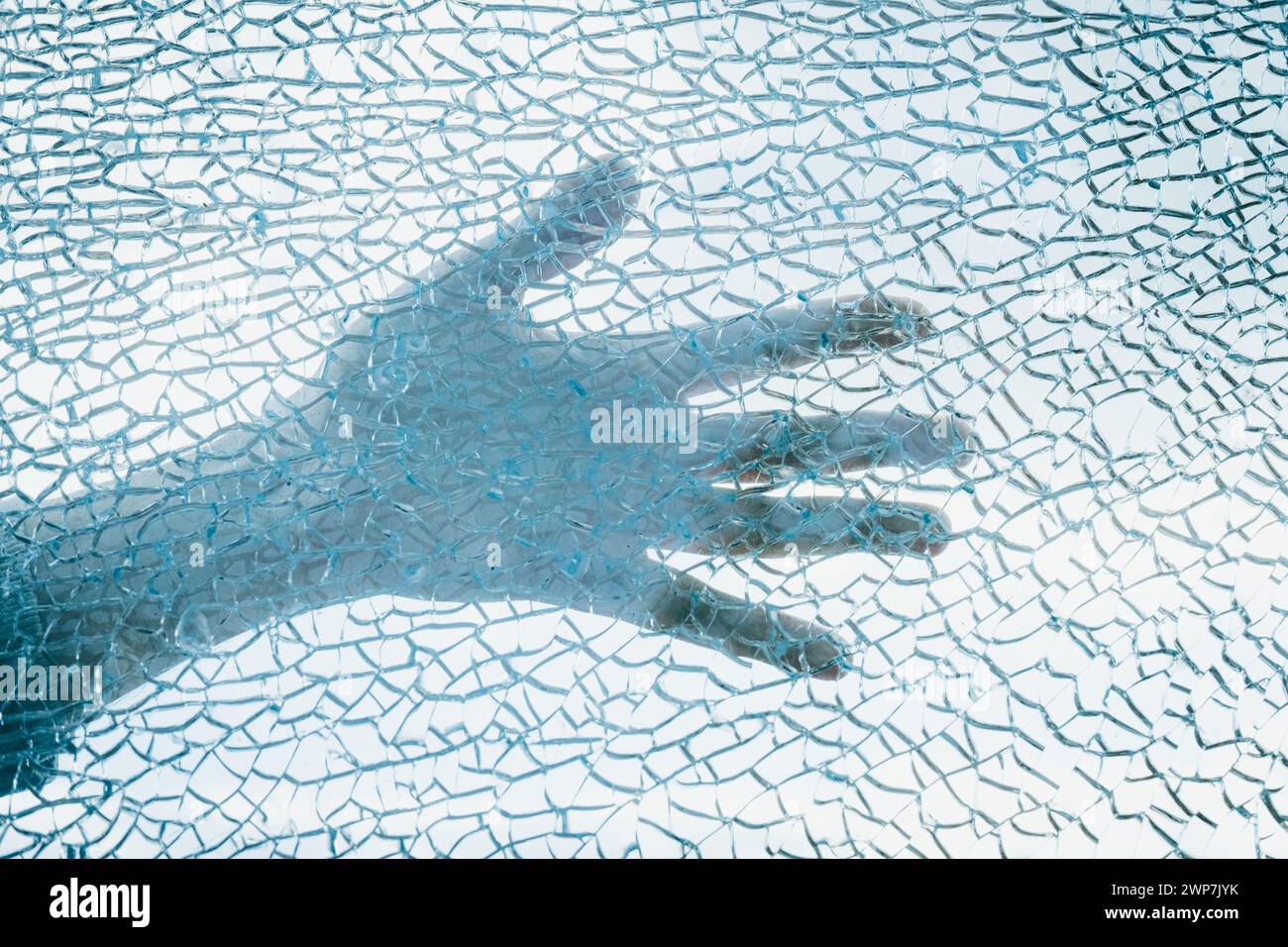 A hand is seen behind a pane of shattered safety glass, creating an ...