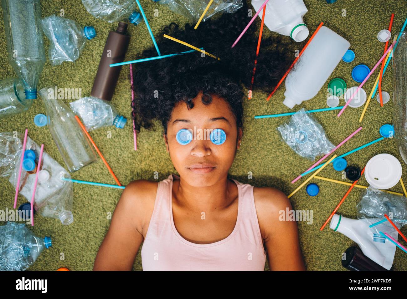 A woman lies amidst a vivid assortment of discarded plastics, using ...