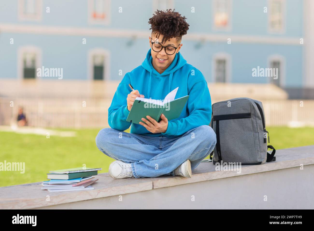 Cheerful young brazilian student guy taking notes learning outside ...