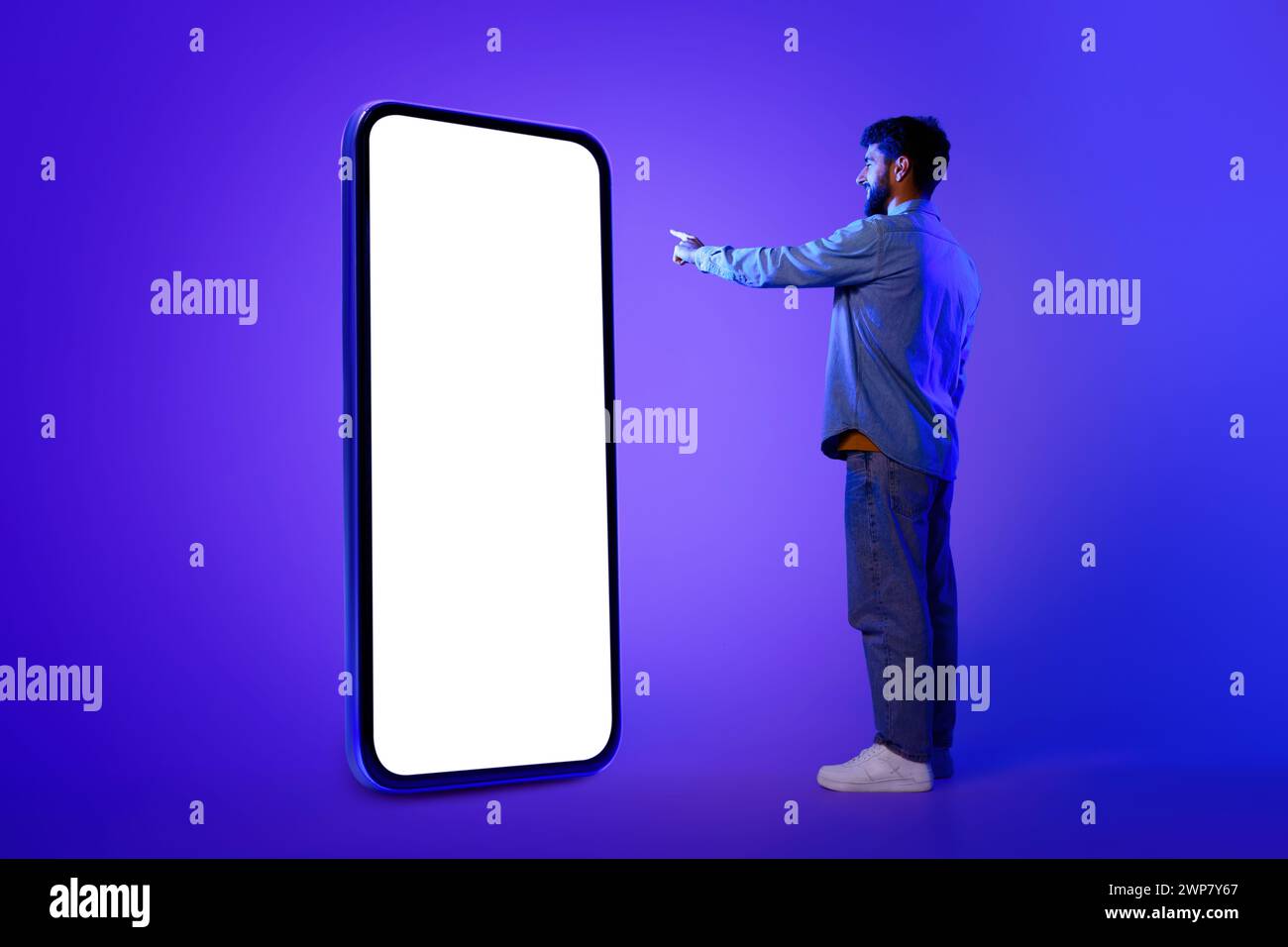 guy stands scrolling on huge smartphone, neon blue studio backdrop ...