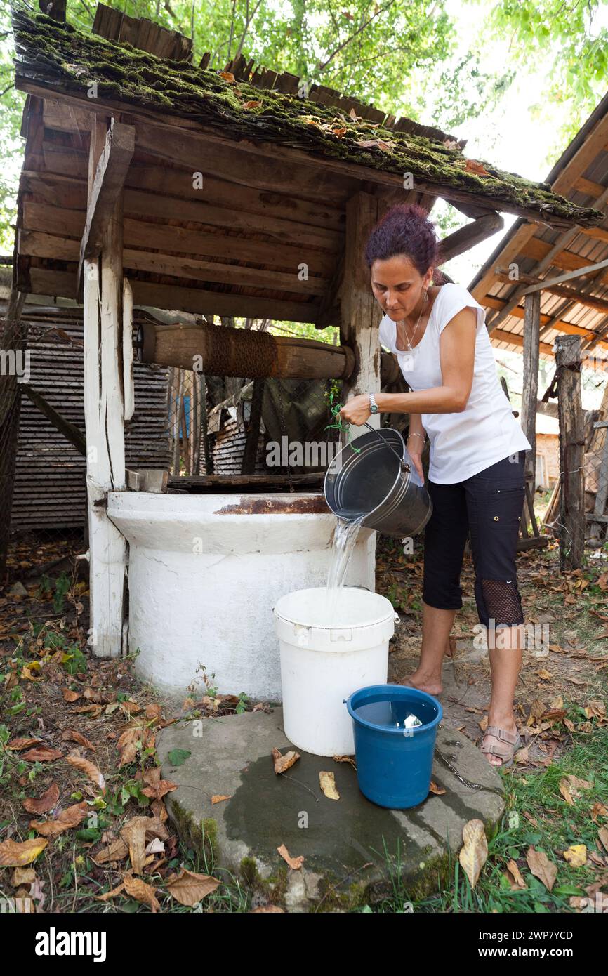 Portrait of a young woman getting water from a vintage wooden well ...