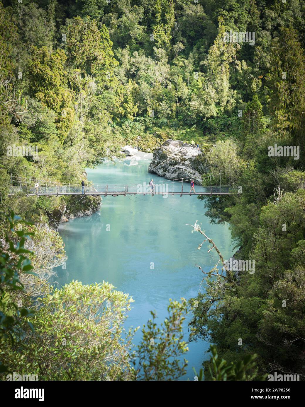 People crossing swing bridge above gorge with azure waters surrounded ...