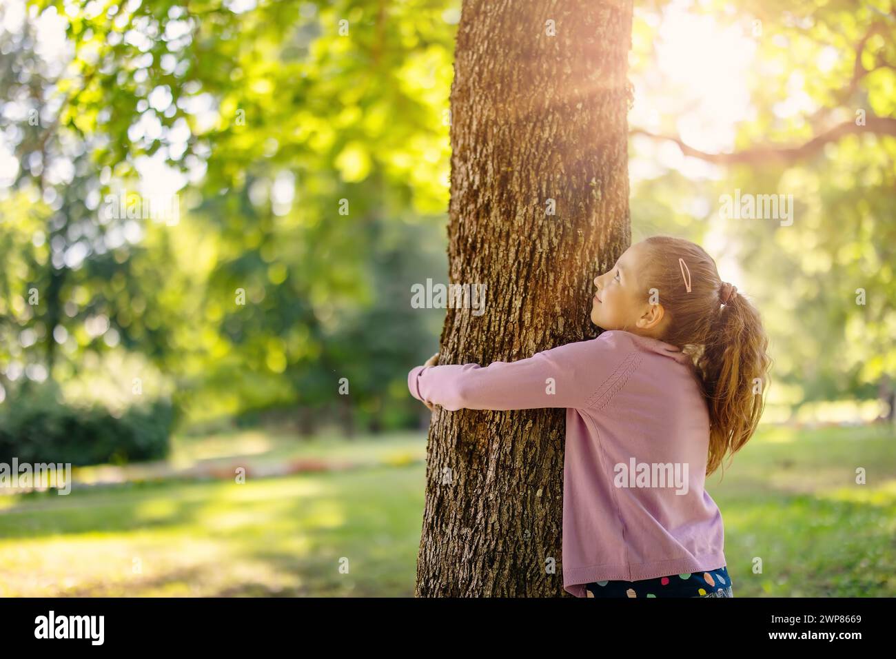 Cute little girl hugging tree in the natural park Stock Photo - Alamy