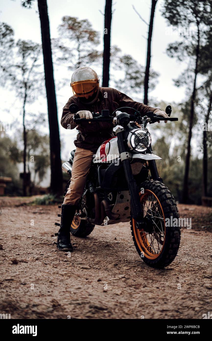 A man in a helmet preparing to ride a motorcycle through forest among ...