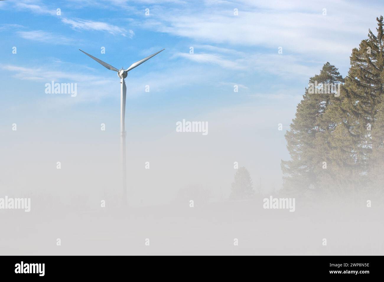 A solitary wind turbine emerges in dense fog, its rotor blades piercing ...