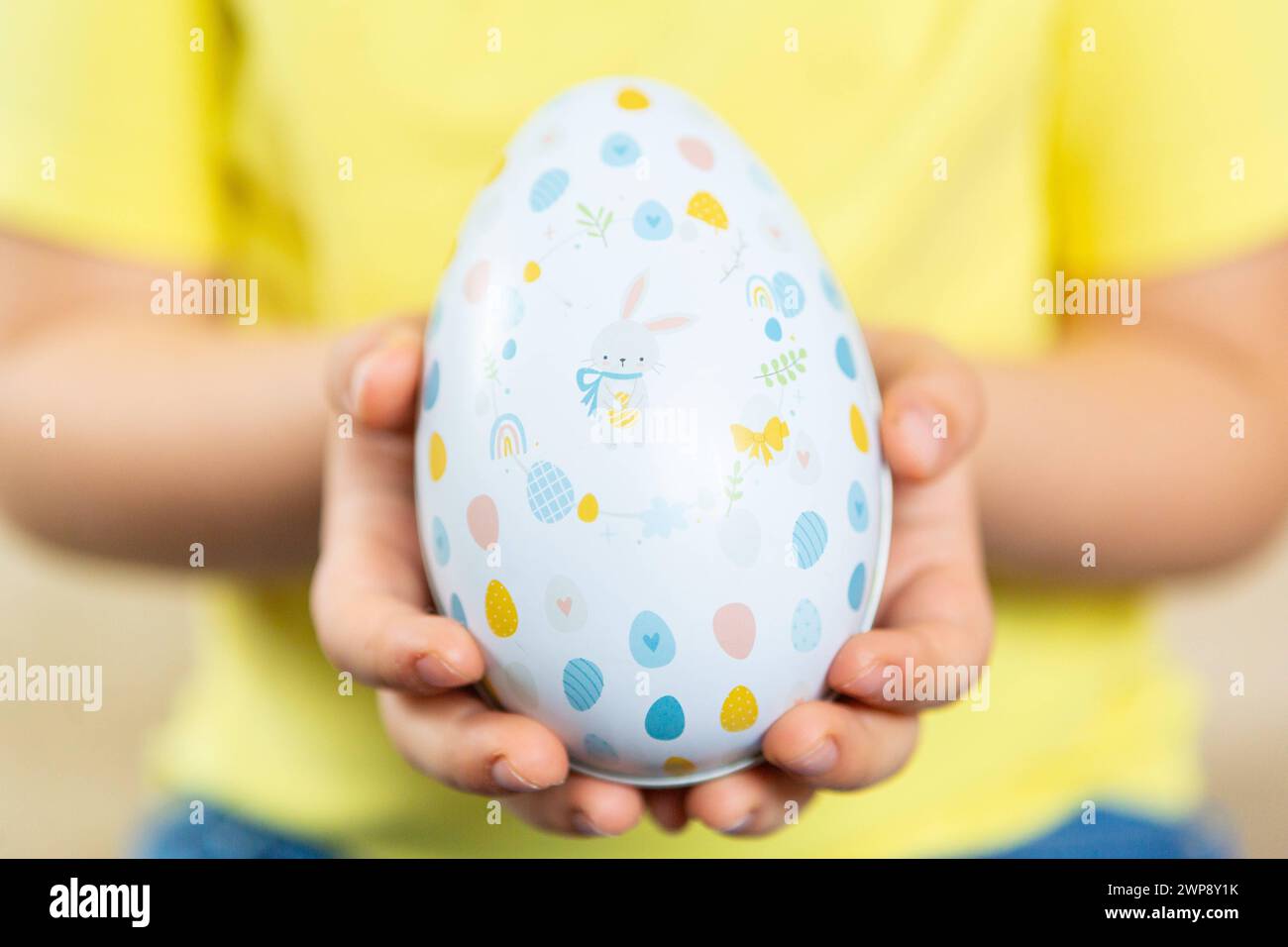 3 March 2024: Child holding a present for Easter. A large egg with ...