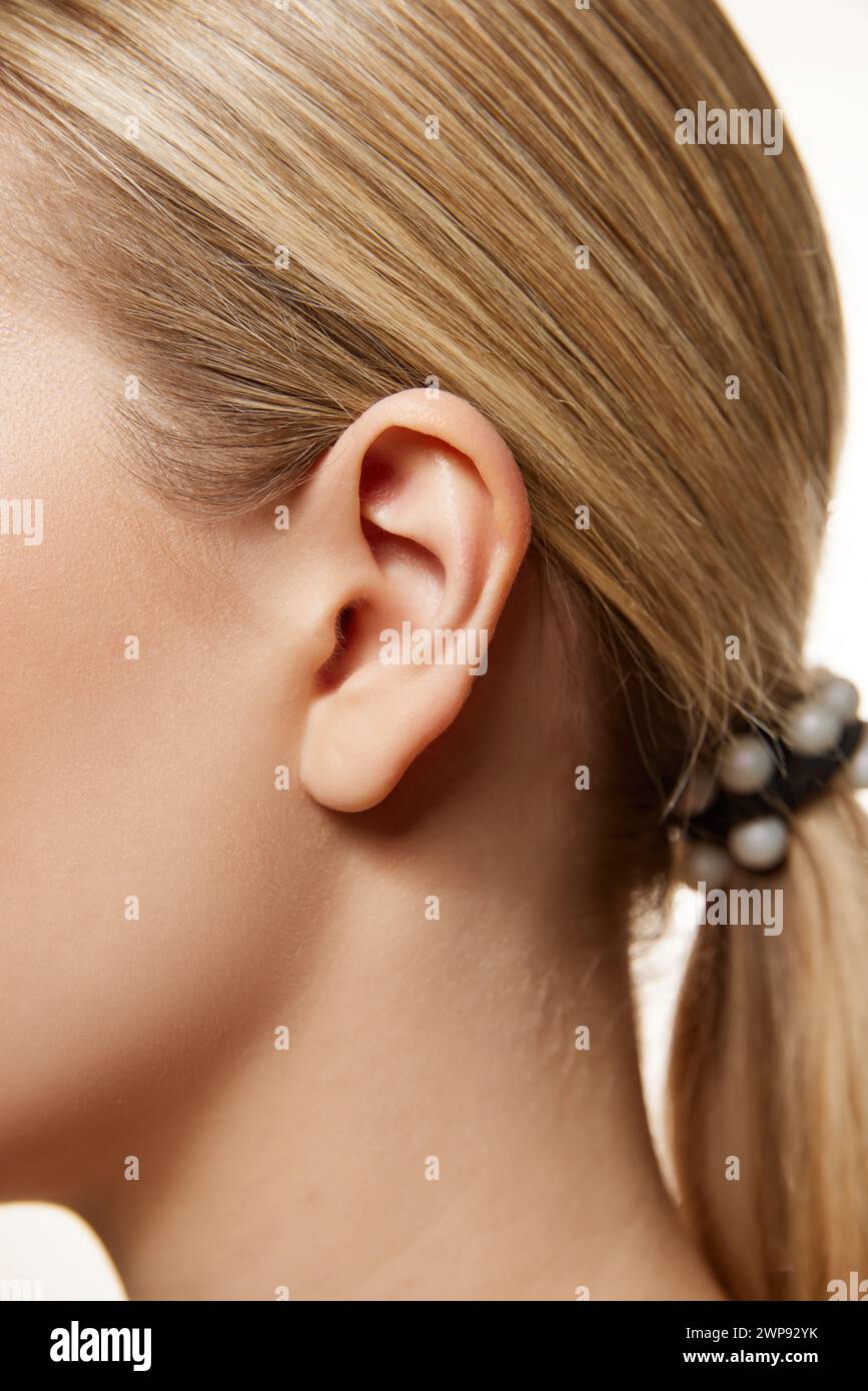 Close-up of a female ear and tied blonde hair isolated against white ...