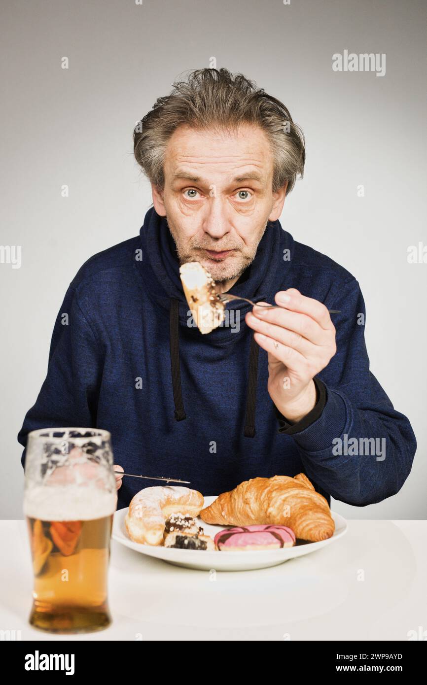 Older man eating sweet pastry and cakes as a meal in studio Stock Photo ...