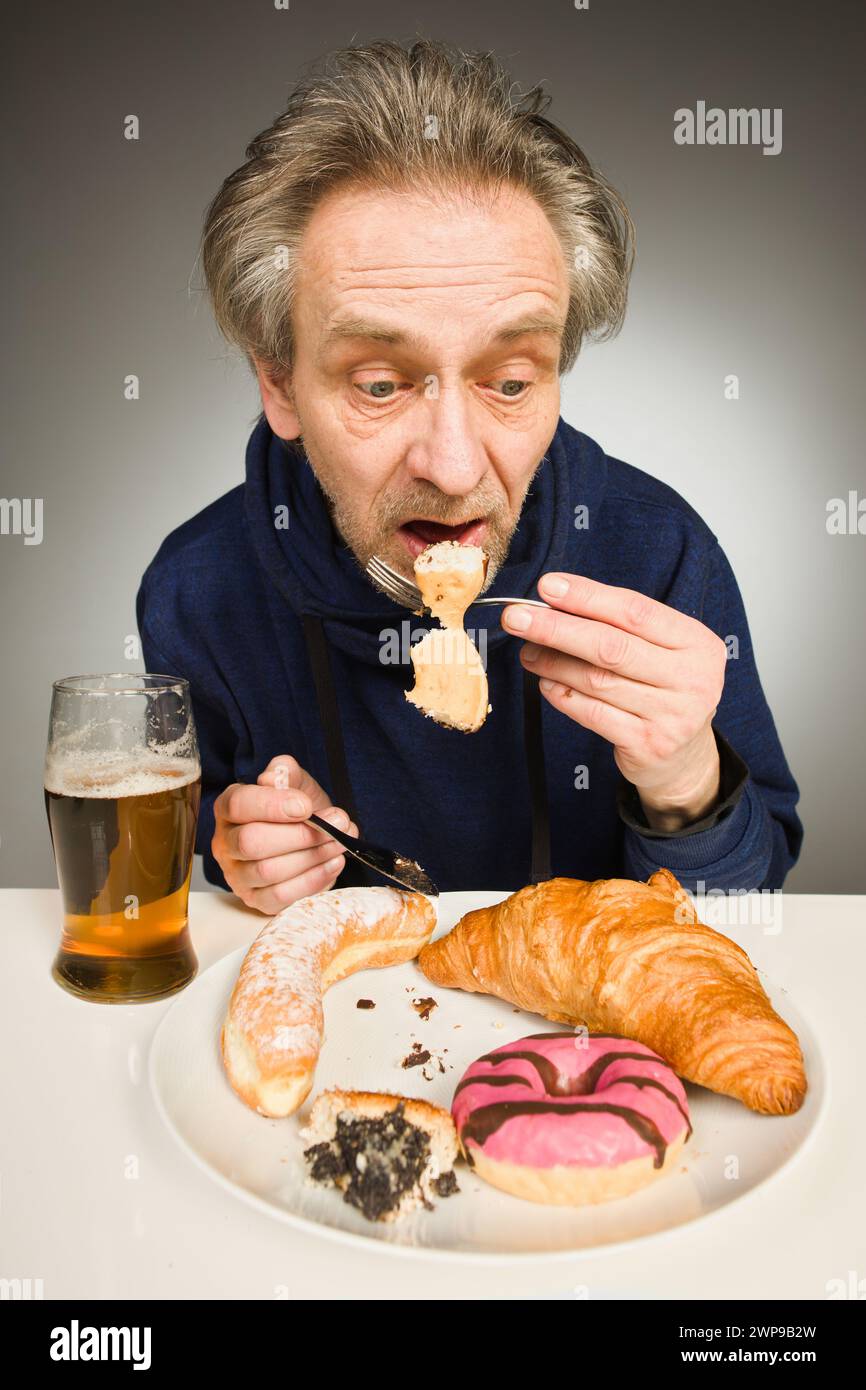 Older man eating sweet pastry and cakes as a meal in studio Stock Photo ...