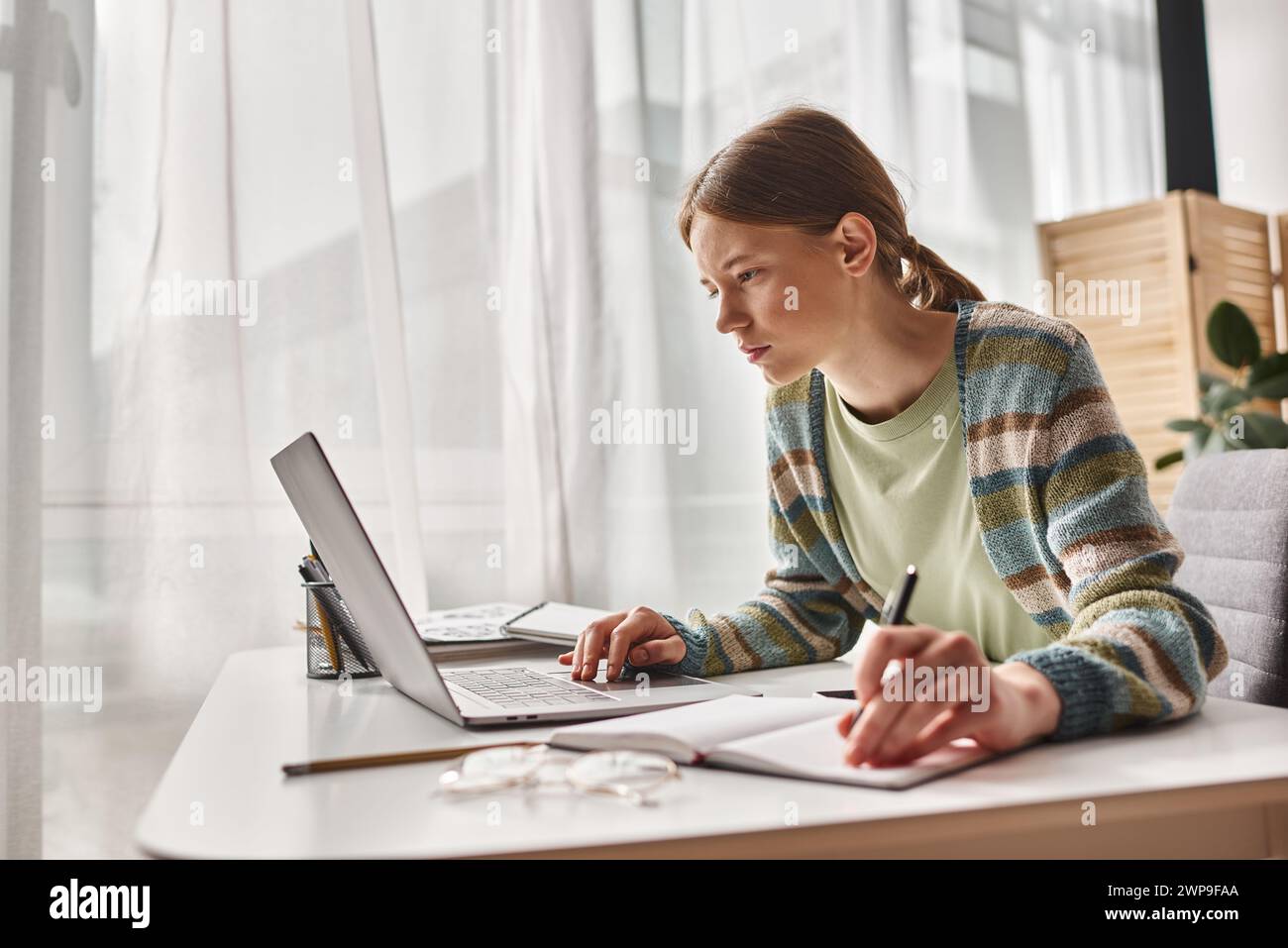 Focused teenager doing homework at home, gen z girl taking notes on ...